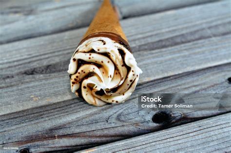 싱싱한 웨이퍼 콘에 초콜릿과 카라멜 소스를 토핑한 빙글빙글 아이스크림 바닐라 콘 분리 웨이퍼 비스킷에 차가운 아이스크림을 녹이는 선택적 초점 여름 휴가 개념 거품 내기에