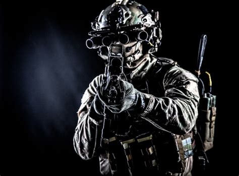 위장 전투복을 입은 특수 부대 병사 로드 캐리어 헬멧 장착된 야간 투시경 전술 무선 헤드셋 카메라에 조준기 조준기가 있는 돌격 소총 조준 낮은 키 스튜디오 촬영