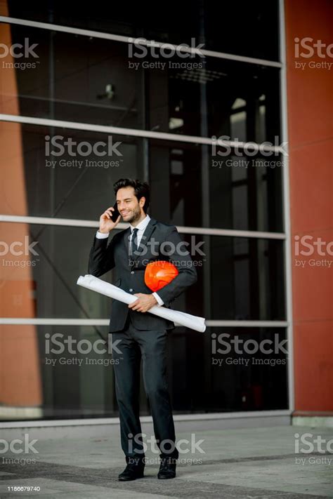 전화를 사용하여 프로젝트와 하드 모자를 가진 젊은 건설 엔지니어 남자 건물 외관에 대한 스톡 사진 및 기타 이미지 건물 외관 건설 산업 건설 현장 Istock