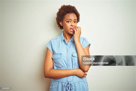 고립 된 배경위에 아프리카 머리를 가진 젊은 아름다운 아프리카 계 미국인 여성은 손톱을 물고 손톱을 물어 뜯는 손에 손을 대고 스트레스를 받고 긴장합니다 불안 문제 감정에