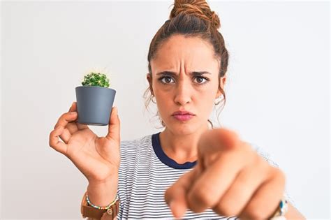 카메라와 당신에 게 손가락으로 가리키는 고립 된 배경 위에 선인장 식물 냄비를 들고 젊은 빨간 머리 여자 손 기호 앞에서 긍정적이 고 자신감 제스처 가리키기에 대한 스톡