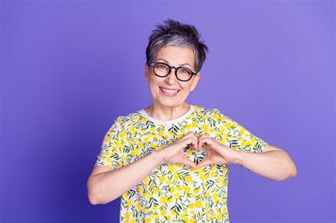 보라색 배경을 배경으로 봄 옷차림을 입고 손으로 하트 제스처를 취하는 미소 짓는 노인 여성 50 54세에 대한 스톡 사진 및 기타 이미지 50 54세 감사 광고