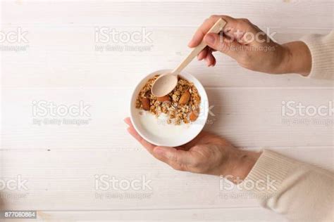 A 그리스 요구르트 주름 진된 손 부드러운 일광 설탕 무료 그 라 놀라 Superfood 시리얼 한 그릇을 들고 베이지색 카디 건 노인 여자의 클로즈업 개념에 대한 스톡