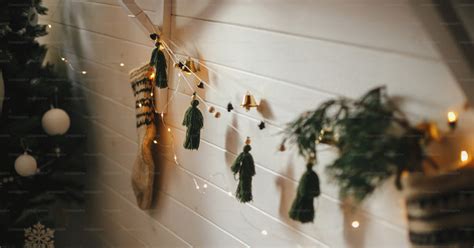 전나무 가지가 있는 크리스마스 소박한 스타킹과 크리스마스 조명이 있는 흰색 나무 벽에 종과 나무가 있는 세련된 화환 축제 장식된 분위기의 스칸디나비아 객실 보호 수제