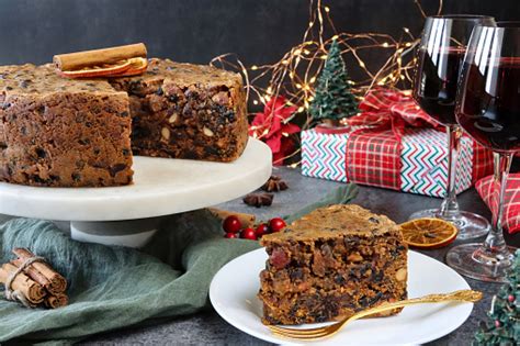 슬라이스 수제 크리스마스 과일 케이크 대리석 케이크 스탠드에 말린 오렌지 감귤류 과일 조각과 계피 스틱을 얹은 이미지 레드 와인 잔 활 녹색 모슬린 접시에 케이크 조각 인공