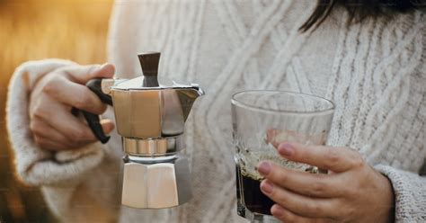 간헐천 커피 메이커와 유리 컵을 들고 시골 시골 허브에서 햇살이 내리쬐는 따뜻한 빛 속에서 신선한 커피를 들고 있는 여행자 분위기 있는 소박한 순간 여행 중 대체 커피