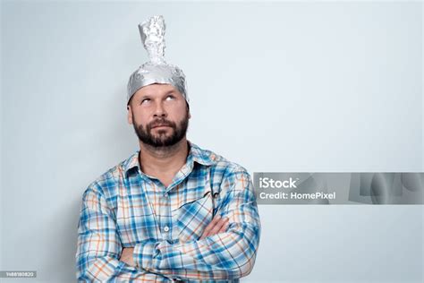 알루미늄 모자를 쓴 격자 무늬 셔츠를 입은 재미있는 수염 난 남자가 밝은 벽 배경 옆에 서서 올려다본다 남자에 대한 스톡 사진 및 기타 이미지 Istock