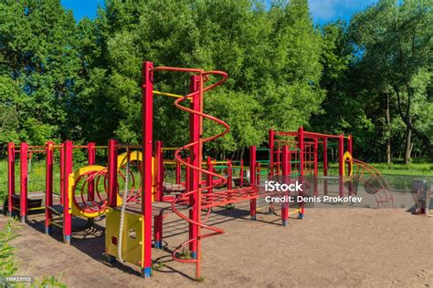 햇빛이 들어오는 아침에 녹색 나무로 둘러싸인 공공 공원의 마당 활동에서 어린이 놀이터 아이들은 현대 놀이터에서 달리고 미끄러지며 스윙하고 시소를 돌봅을 이룬다 도시 이웃