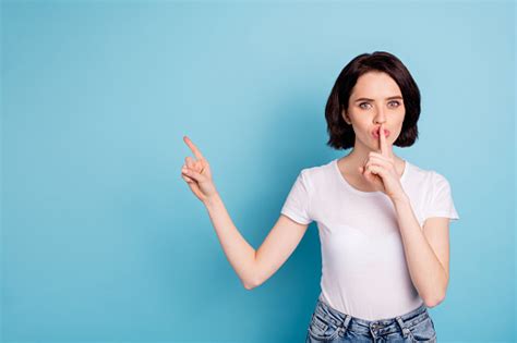 그녀의 초상화 그녀의 좋은 매력적인 사랑스러운 자신감 신비한 소녀는 밝은 선명한 빛 선명한 푸른 청록색 색상 배경에 고립 된 Shh 기호를 보여주는 옆으로 가리키는