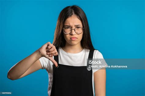 젊은 아시아 소녀 서 블루 스튜디오 배경 에 불만을 표현 하 고 카메라에 엄지 손가락 아래로 제스처를 보여주는 혐오의 표시와 여성의 초상화 동양인에 대한 스톡 사진 및 기타