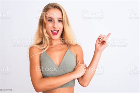 고립된 흰색 배경 위에 서있는 캐주얼 한 녹색 티셔츠를 입은 젊은 아름다운 여성은 얼굴에 큰 미소를 지으며 카메라를 바라보는 옆구리를 손가락으로 가리킵니다 T 셔츠에 대한