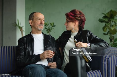 시니어 아버지는 로프트 스타일의 방에서 파란색 소파에 앉아있는 성인 딸과 함께 술을 마시고 남자는 위스키 잔을 들고 여자는