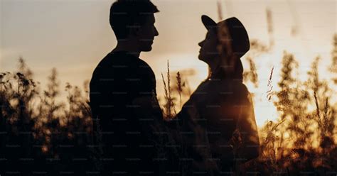 세련된 임신한 부부는 잔디 사이에 있는 가을 공원에서 햇살이 내리쬐는 실루엣을 가지고 있다 행복한 젊은 부모 엄마와 아빠 아기 범프를 껴안고 일몰에 아름다운 순간을