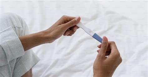 젊은 아프리카계 미국인 여성의 잘린 보기는 두 개의 빨간색 줄무늬가 있는 긍정적인 임신 빠른 플라스틱 테스트를 들고 여성이