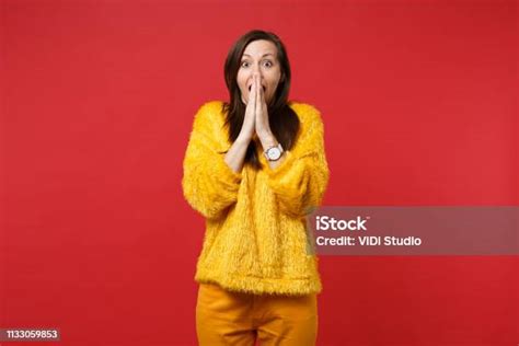 스튜디오에서 밝은 빨간색 벽 배경에 고립 된 손으로 입을 덮고 노란 모피 스웨터에 놀란 젊은 여자의 초상화 사람들은 진심으로 감정 라이프 스타일 개념입니다 복사 공간을 모의
