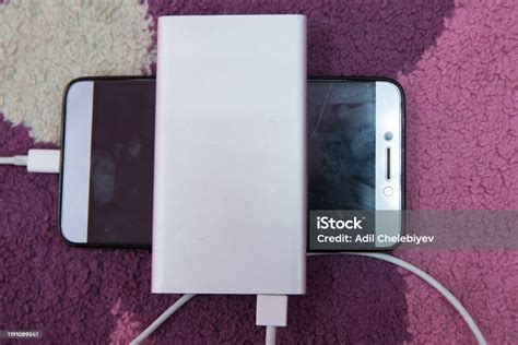 나선형 Usb 케이블을 통해 실버 파워 뱅크와 스마트 폰 충전 분홍색 카펫에 전원 뱅크로 충전하는 스마트 폰 에너지 뱅크로 전화 충전 Usb 케이블에 대한 스톡 사진 및
