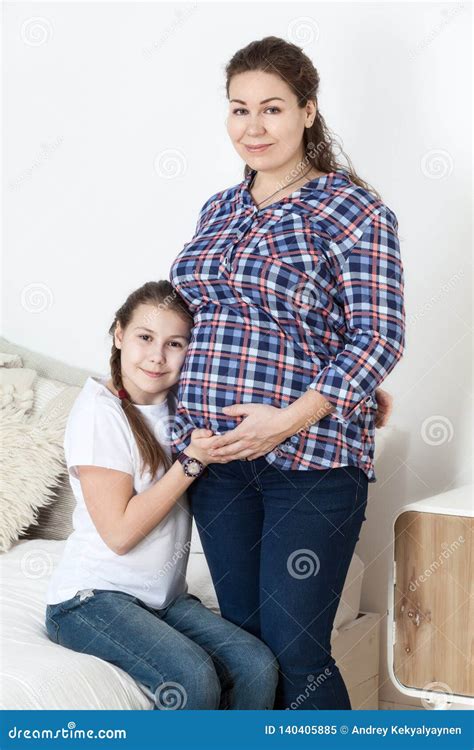 Portrait Of Pregnant Mother With Young Daughter Listening The Belly