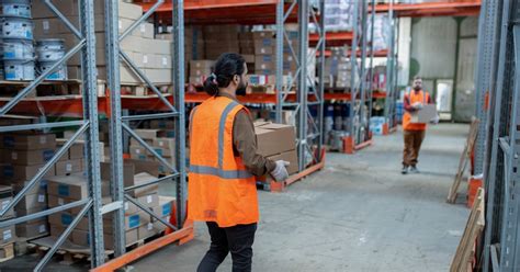 반사 조끼를 입은 보관 작업자가 금속 프레임 선반이 있는 창고에서 품목을 분배하는 동안 상자를 이동합니다 사진 Unsplash의 러시아 이미지