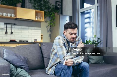 기분이 좋지 않습니다 잘 생긴 젊은 남자가 집에서 소파에 앉아 아프고 춥고 춥고 흔들리고 열이 난다 그는 손으로 자신을 안아줍니다 그는 따뜻하게 지내고 싶어합니다 남자에