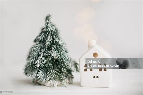 흰색 배경에 황금 빛 보케와 크리스마스 작은 집과 나무 축제 분위기의 현대적인 장식 즐거운 휴일 보내세요 미니어처 아늑한 집과 수제 소나무 메리 크리스마스 인사말 개념에