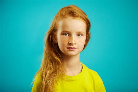 친절과 정직의 진지한 모양과 귀여운 어린이 소녀의 수평 샷 빨간 머리 아름 다운 주 근 깨 노란색 T 셔츠를 착용 고립 된 파란색에 아이의 초상화 빨간 머리에 대한 스톡