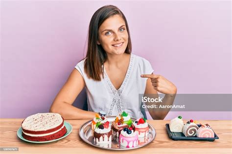 젊은 백인 여자 먹는 패스트리 가리키는 손가락 에 한 자기 미소 행복 하 고 자랑 가리키기에 대한 스톡 사진 및 기타 이미지 가리키기 긍정적인 감정 표현 놀라움