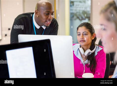 Community College Instructor Helping Student At Computer In Classroom