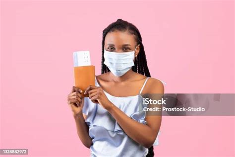 보호 얼굴 마스크를 쓰고 분홍색 배경에 여권과 비행기 티켓을 들고 있는 아프로 무리를 가진 행복한 흑인 여성 쥠에 대한 스톡 사진 및 기타 이미지 Istock