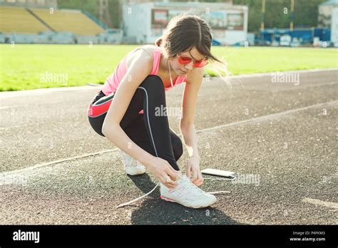 Beautiful Teenage Girl Running In Stadium Tying Laces Of Running Shoes
