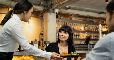 젊은 인종 간 커플 사람들이 실내 식당에 앉아 점심을 먹기 위해 함께 음식을 먹고 있습니다 여성 웨이트리스로부터 음식을 받는 여성 고객 그들은 행복을 느끼며 식사를