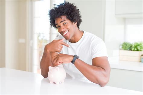 아프리카계 미국인 남자 퍼 팅 A 동전 내부 돼지 저금통 와 깜짝 얼굴 가리키는 손가락 에 자신 가리키기에 대한 스톡 사진 및 기타 이미지 Istock