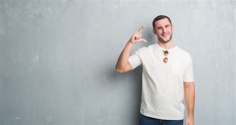 젊은 백인 남자 선글라스 미소와 자신감 보면서 손가락과 카메라 크기 표시를 하 고 손으로 몸짓을 입고 회색 그런 지 벽에 측정 개념입니다 개념에 대한 스톡 사진 및 기타