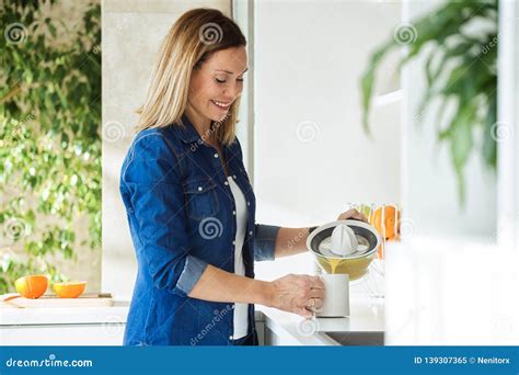 Attractive Mother Making A Freshly Squeezed Orange Juice With The Help Of A Citrus Juicer On A