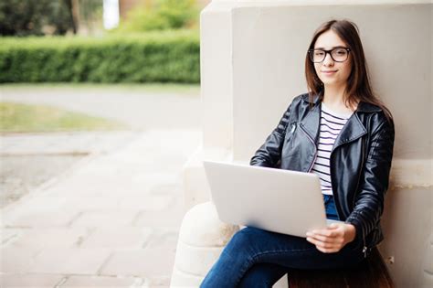 앉아 노트북으로 웃는 여자 대학 캠퍼스 파크에서 풀밭에 다리를 건너 캐주얼 여성 학생 컴퓨터와 시험을 준비입니다 교육 및 기술 개념입니다 검색에 대한 스톡 사진 및 기타