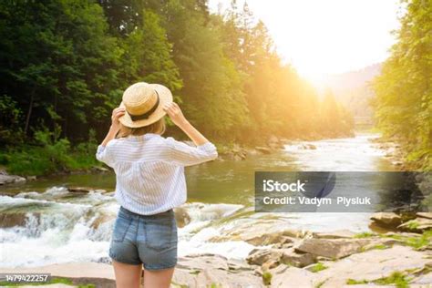 아름다운 힙스터 소녀가 주변의 산을 즐기고 있다 반바지와 밀짚모자를 쓴 여자가 강 근처의 바위 위에 서 있다 여름 분위기 방랑벽과 여행 개념 강에 대한 스톡 사진 및 기타