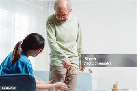 간병인과 물리 치료를하는 아시아 노인 환자 휠체어에서 일어나 집에서 보행기로 걷는 연습을 돕는 여성 간호사는 요양원에서 천천히 산책을 연습합니다 25 29세에 대한 스톡
