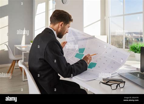 Businessman Analyzing Cadastral Map While Sitting At Desk In Office