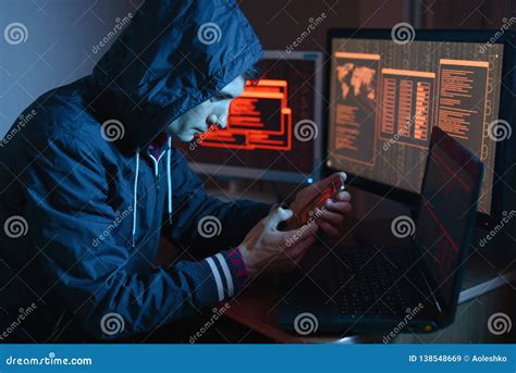 Hacker In The Hood Holding The Phone In His Hands Trying To Hack The