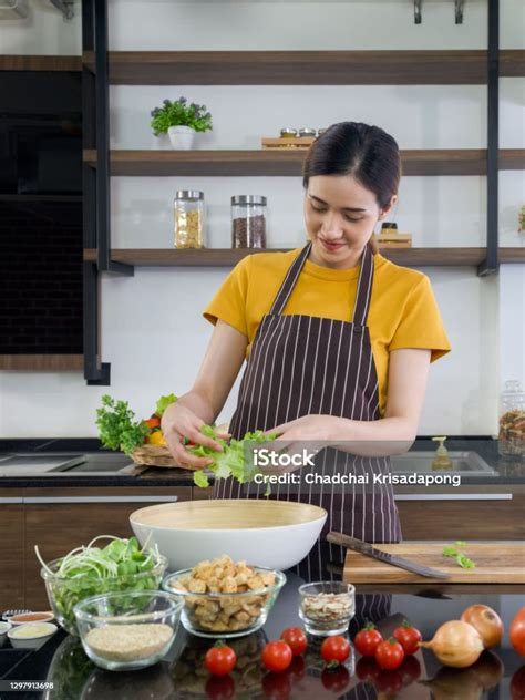 앞치마를 입은 아시아 주부는 채소를 샐러드 그릇에 넣고 손으로 섞는다 현대적인 주방에서 아침 분위기 25 29세에 대한 스톡 사진 및 기타 이미지 Istock