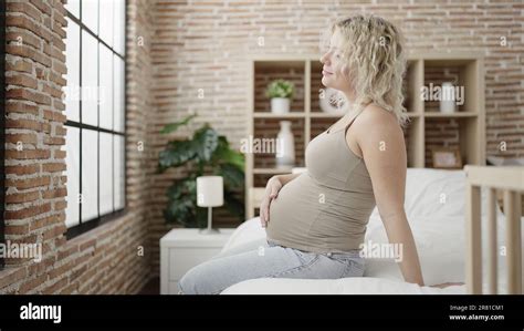 Young Pregnant Woman Touching Belly Sitting On Bed At Bedroom Stock