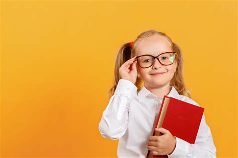 노란색 배경에 귀여운 어린 소녀의 초상화입니다 카메라를 보고 책을 들고 안경을 곧게 펴는 여학생 교육의 개념 공간을 복사합니다 개념에 대한 스톡 사진 및 기타 이미지