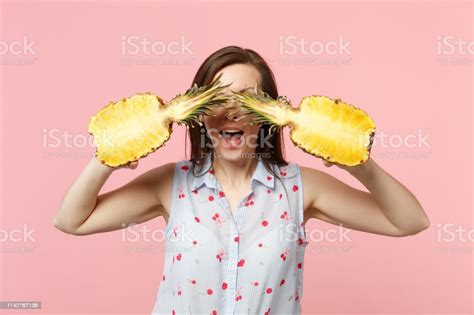 분홍색 파스텔 벽 배경에 고립 된 신선한 잘 익은 파인애플 과일의 Halfs와 눈을 덮고 있는 여름 옷을 들고 젊은 여자 사람들은 생생한 라이프 스타일 휴식 휴가 개념입니다