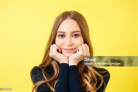 긴 머리를 가진 젊고 아름다운 매력적인 귀여운 십대 소녀 소녀 모델의 초상화는 스튜디오의 노란색 배경에 턱 옆에서 손을 잡고 있습니다 16 17 살에 대한 스톡 사진 및