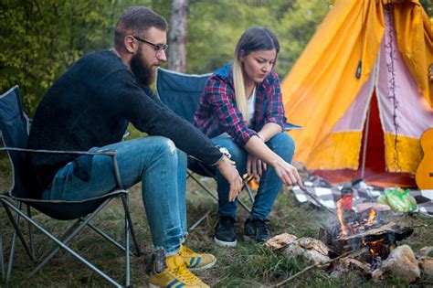 아름 다운 커플 앉아 캠프 파이어 주위에 캠핑 텐트와 배경에 남자 막대기로 화재 제스처 2명에 대한 스톡 사진 및 기타 이미지 Istock