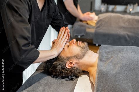 Two Masseurs Doing Facial Massage To A Couple At Spa Salon Wellness