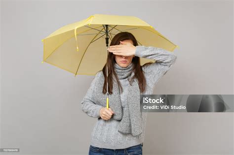 노란 우산을 들고 회색 스웨터 스카프 손으로 눈을 덮고 있는 젊은 여자는 회색 벽 배경에 고립 건강 패션 라이프 스타일 사람 감정 추운 계절 개념입니다 복사 공간을 비웃는