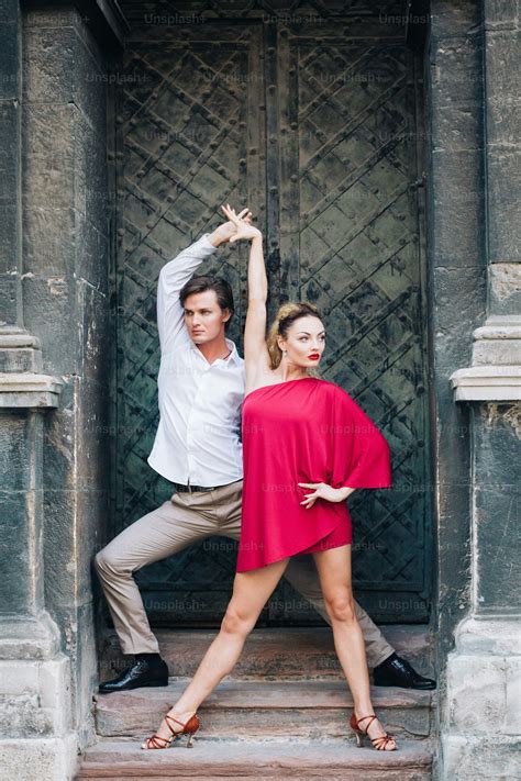 햇볕이 잘 드는 거리의 오래된 건물에서 포옹하고 춤을 추는 사랑에 빠진 아름다운 행복한 커플 세련된 힙스터 신랑과 빨간 드레스를 입은 금발 신부는 춤을 추고 전문 댄서들