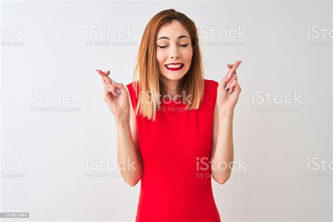 고립 된 흰색 배경 몸짓 손가락 위에 서있는 우아한 빨간 드레스를 입은 빨간 머리 사업가가 희망과 눈을 감고 미소를 지었습니다 행운과 미신 개념 귀여운에 대한 스톡 사진 및