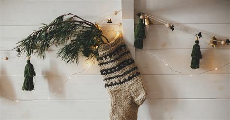 전나무 가지가 있는 크리스마스 소박한 스타킹과 크리스마스 조명이 있는 흰색 나무 벽에 종과 나무가 있는 세련된 화환 축제 장식된 분위기의 스칸디나비아 객실 현대적인 수제