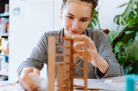 Young Attractive Woman Assembling Wooden Model At Table In Bright Room With House Plants Stock